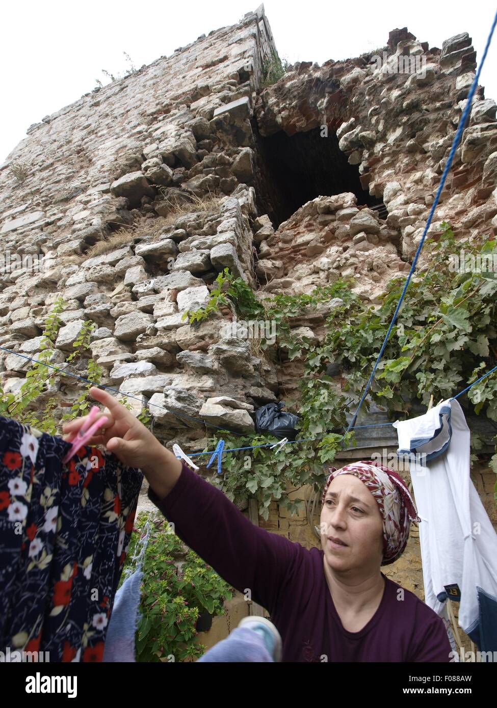 Woman pinning clothes on clothesline and stone wall in background in ...