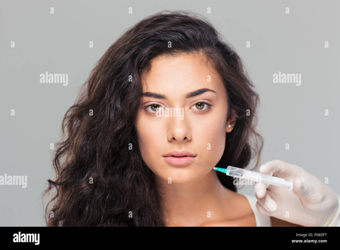 Young woman getting cosmetic injection of botox over gray background ...