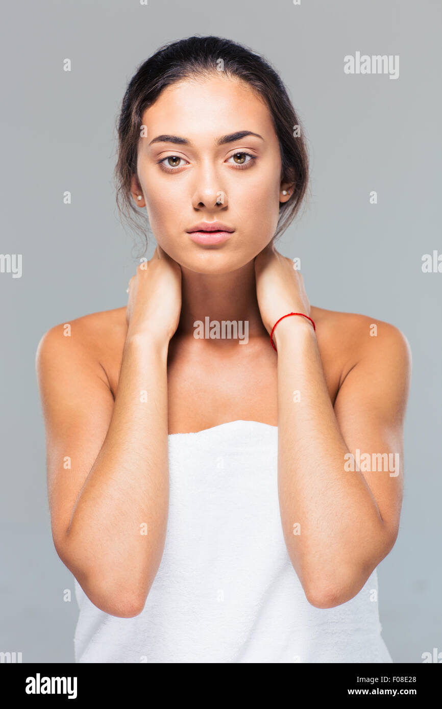 Portrait of a beautiful woman standing in towel over gray background ...
