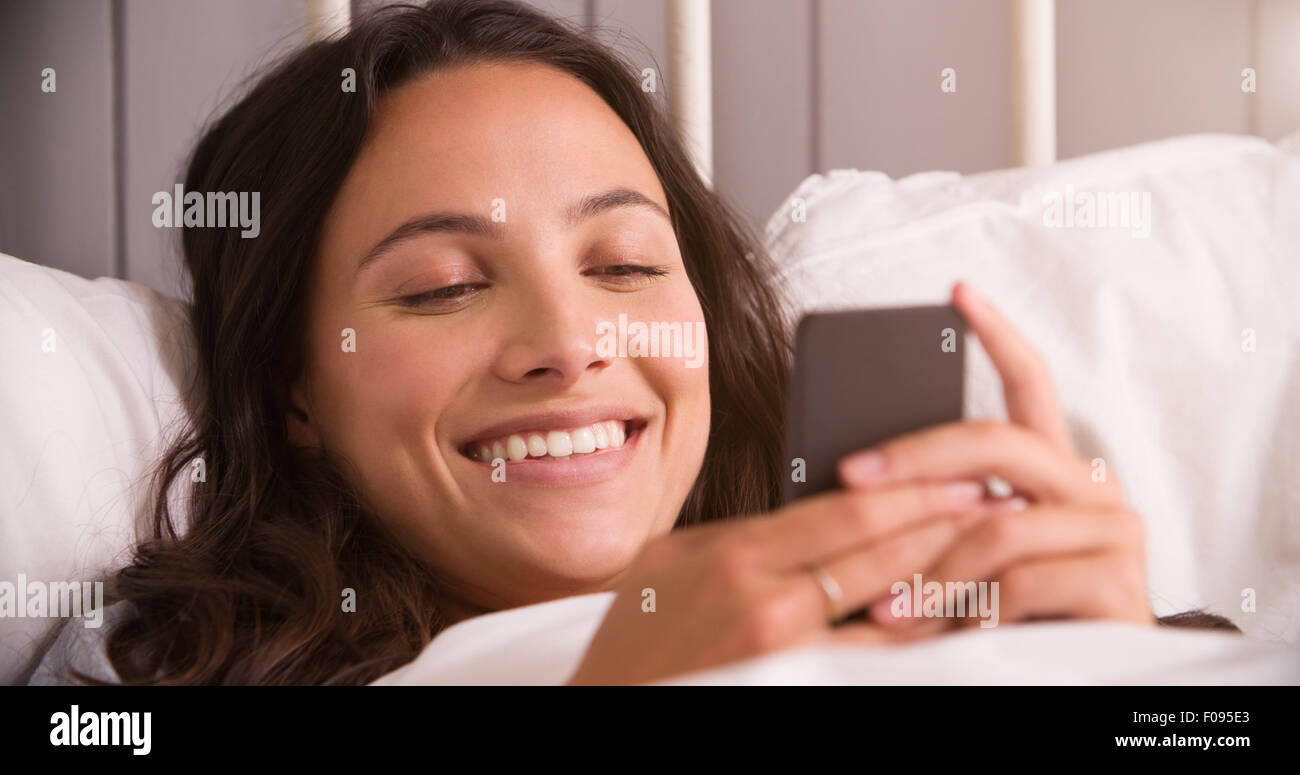 Woman Lying In Bed Checking Messages On Mobile Phone Stock Photo - Alamy