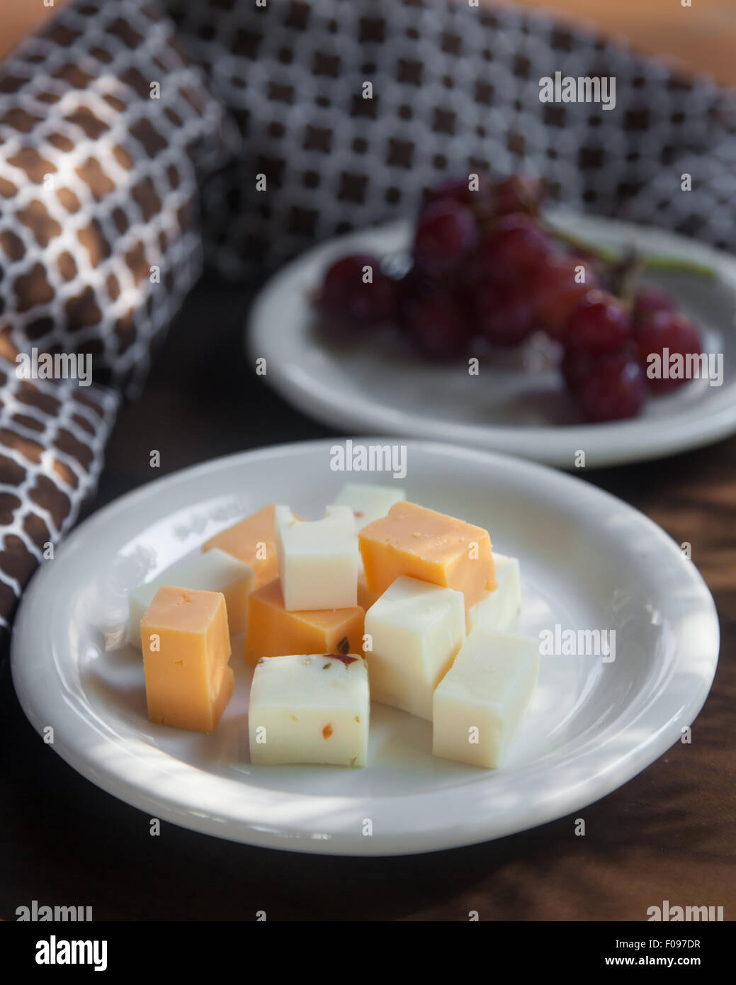 A white plate of various cubed cheeses sits atop a brown wooden ...