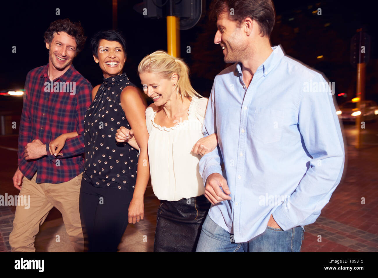 Four friends walking through town together at night Stock Photo - Alamy