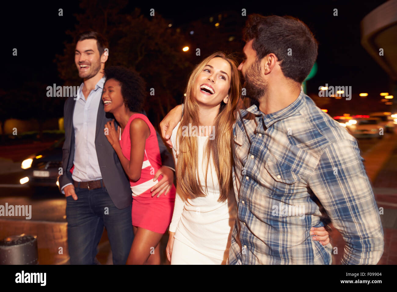 Four friends walking through town together at night Stock Photo - Alamy