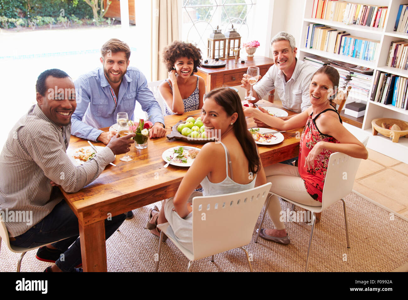 Friends sitting at a dining table looking at the camera Stock Photo - Alamy