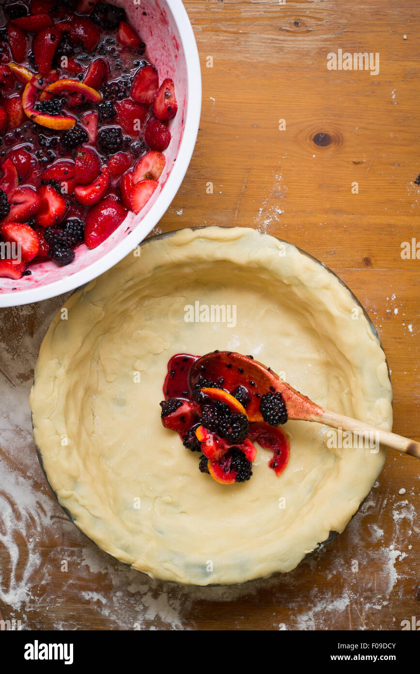 Overhead view of pie filling being scooped into uncooked pie crust ...