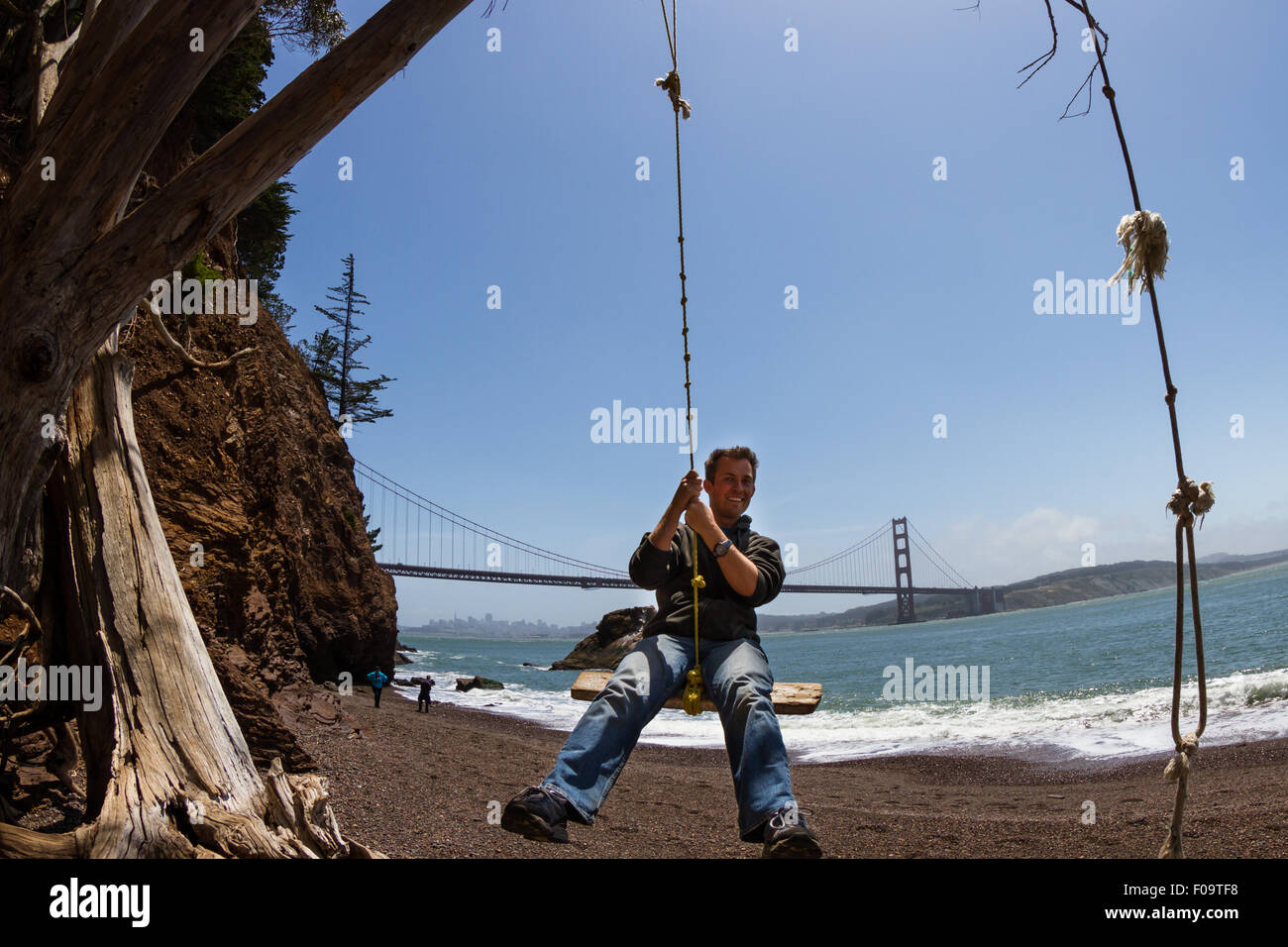 young man swinging on a piece of wood tied with a rope with the Golden ...