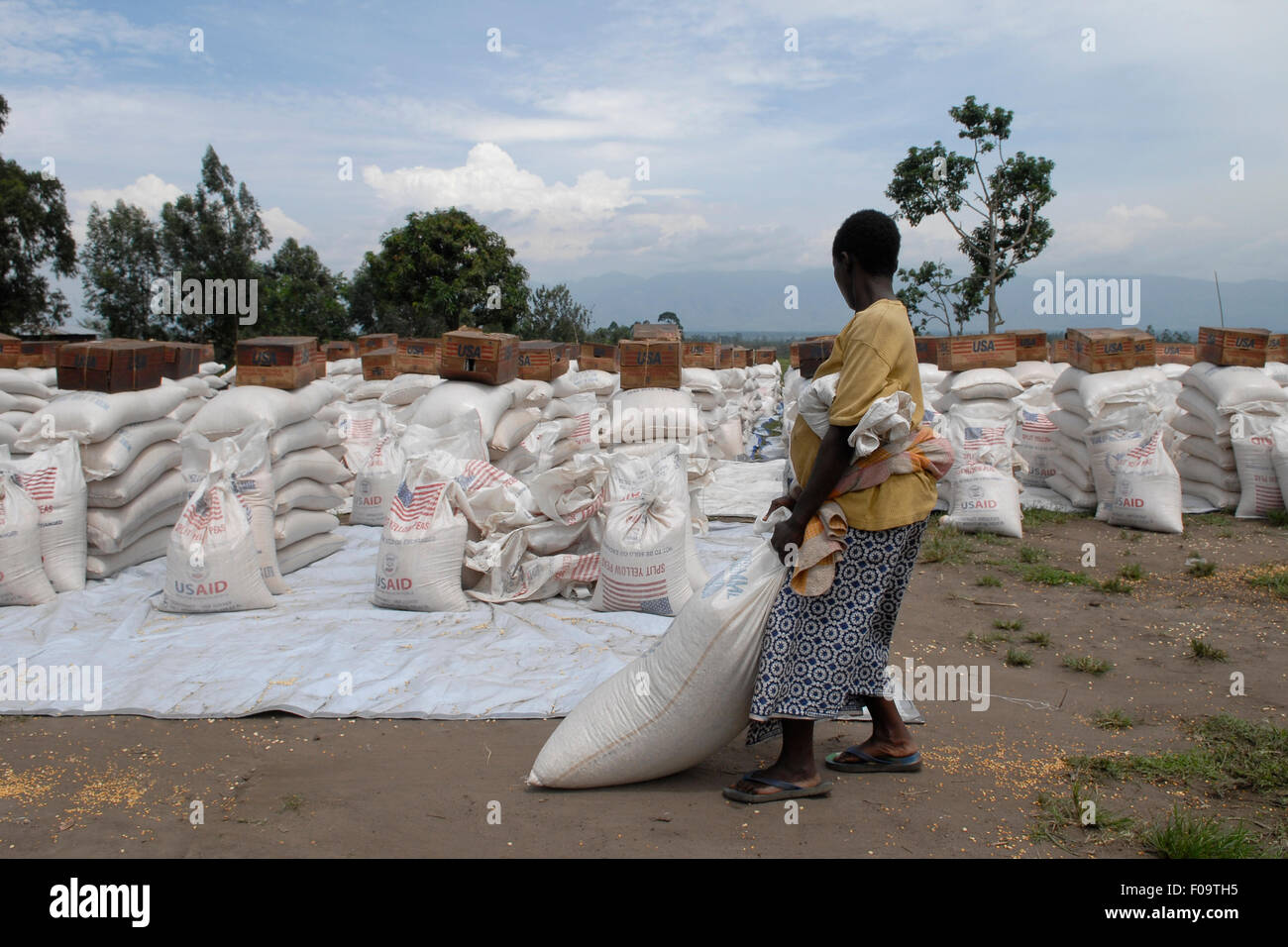 A displaced Congolese woman drags a heavy sack of corn soya blend ...