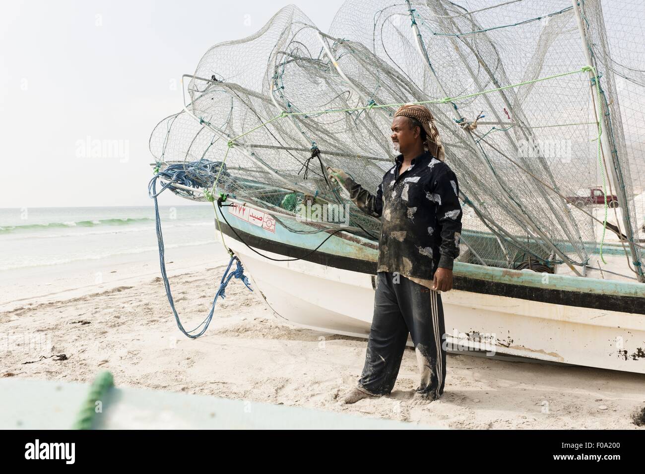Fisherman standing beside fishing boat on Maghsail beach, Salalah, Oman ...
