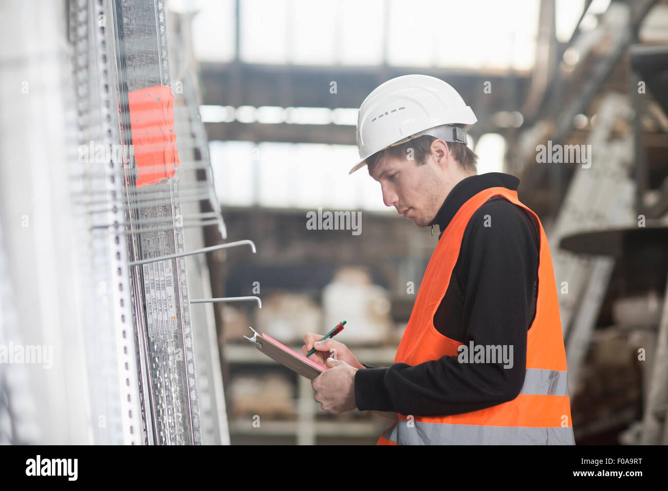 Young male warehouse worker stock taking with clipboard in warehouse ...