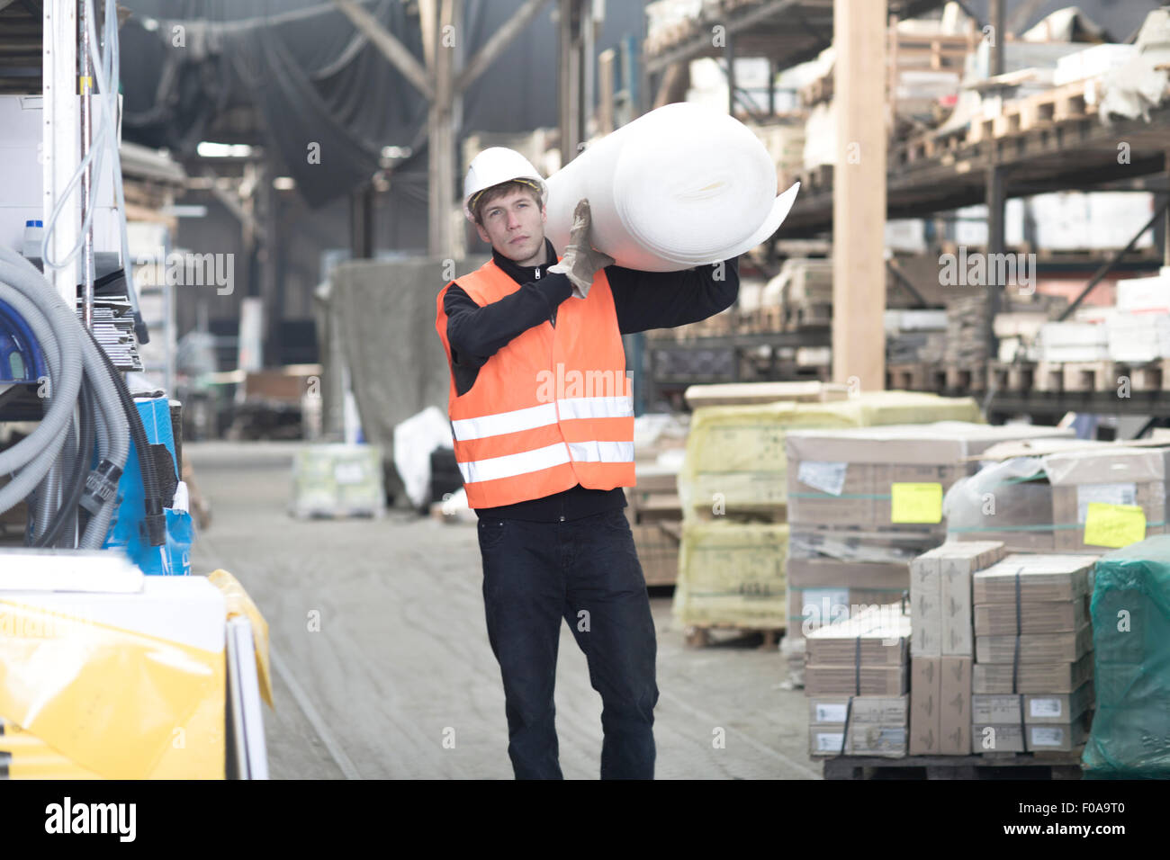 Young male warehouse worker carrying polystyrene roll on shoulder Stock ...