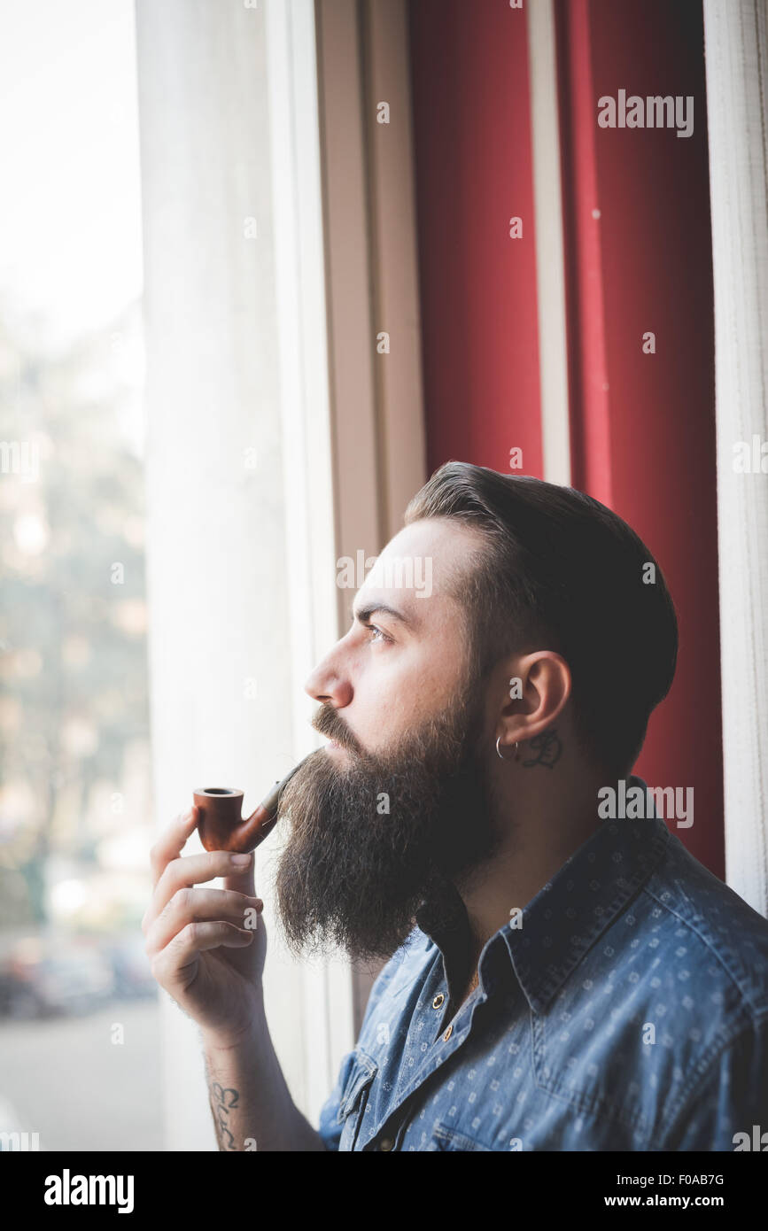 Young bearded man smoking pipe by window Stock Photo - Alamy