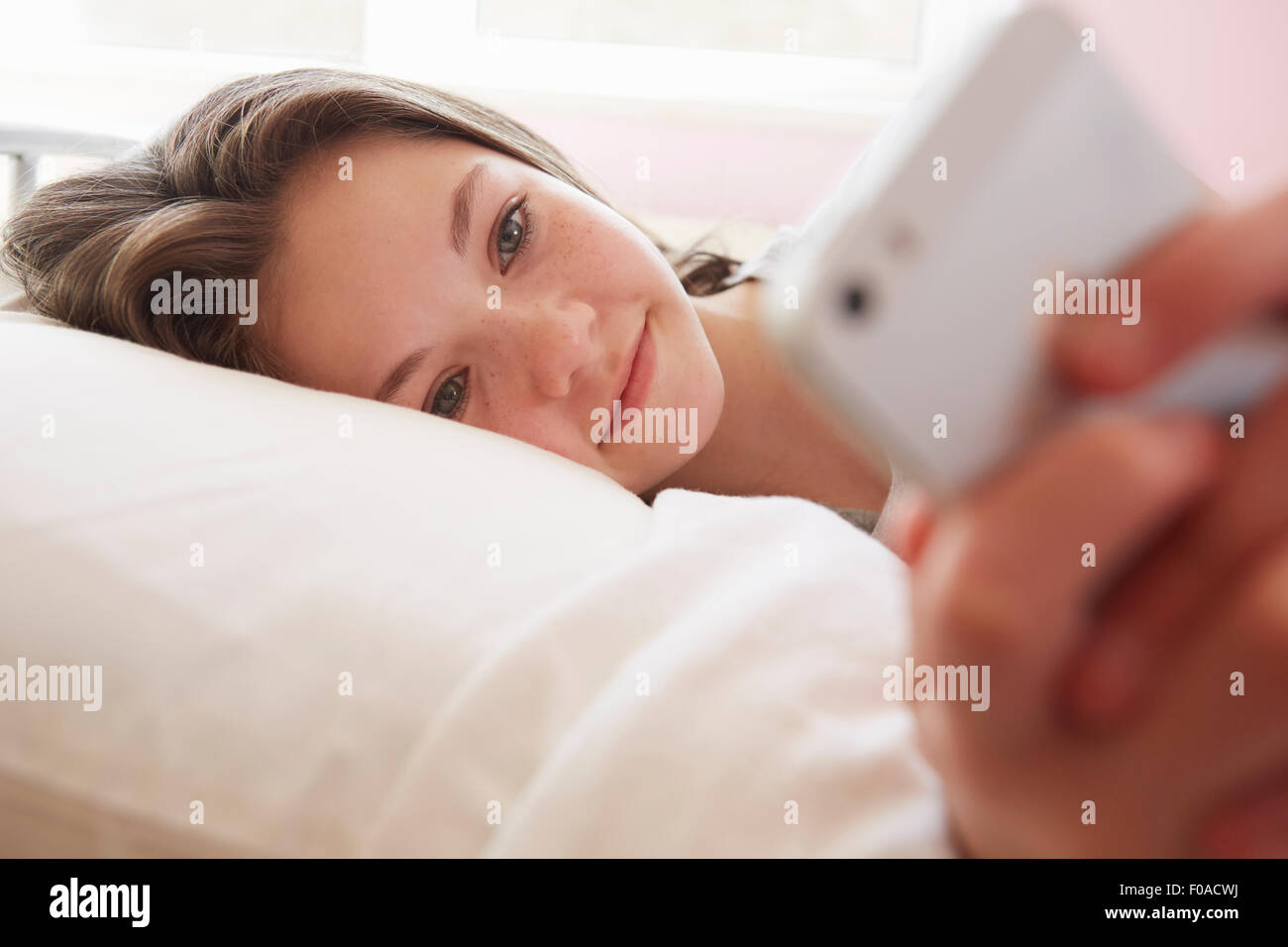 Girl lying on bed texting on smartphone Stock Photo - Alamy