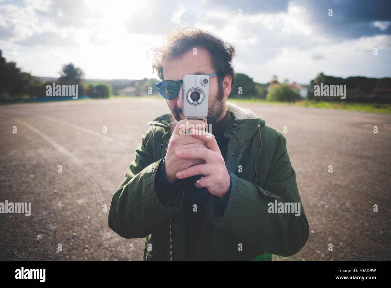 Portrait of mid adult man pointing vintage movie camera on waste ground ...