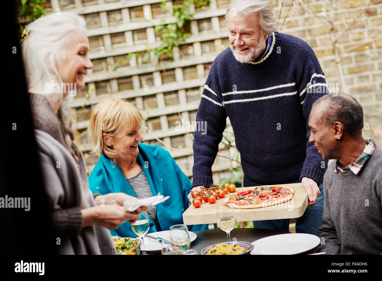 Senior man serving friends pizza in garden Stock Photo - Alamy