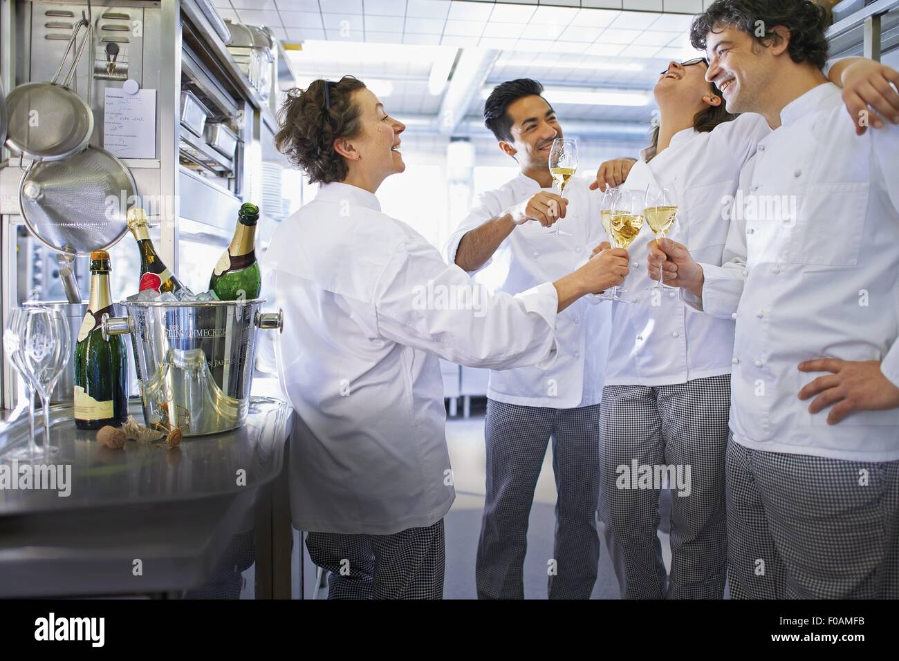 Laughing chefs and holding wine glasses while toasting in kitchen Stock ...