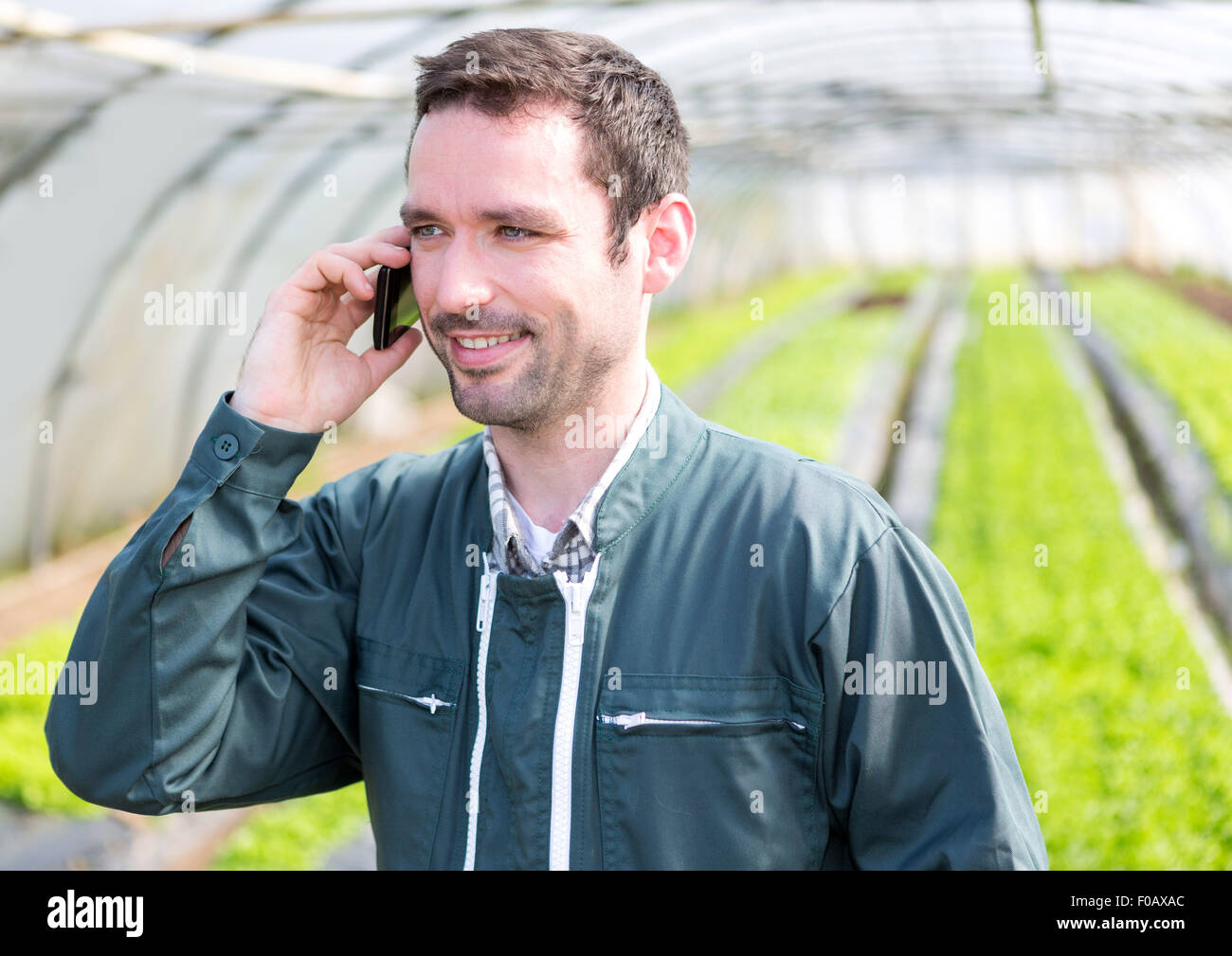 View of a Portrait of an attractive farmer in a greenhouse using mobile ...