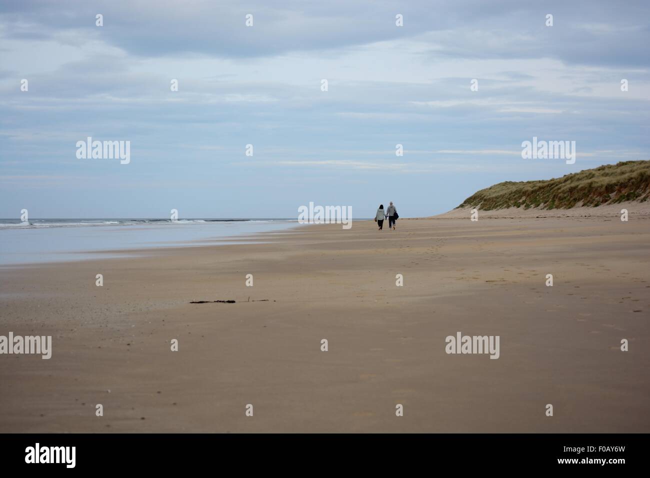 A couple walking along a deserted wide expansive beach in North East ...