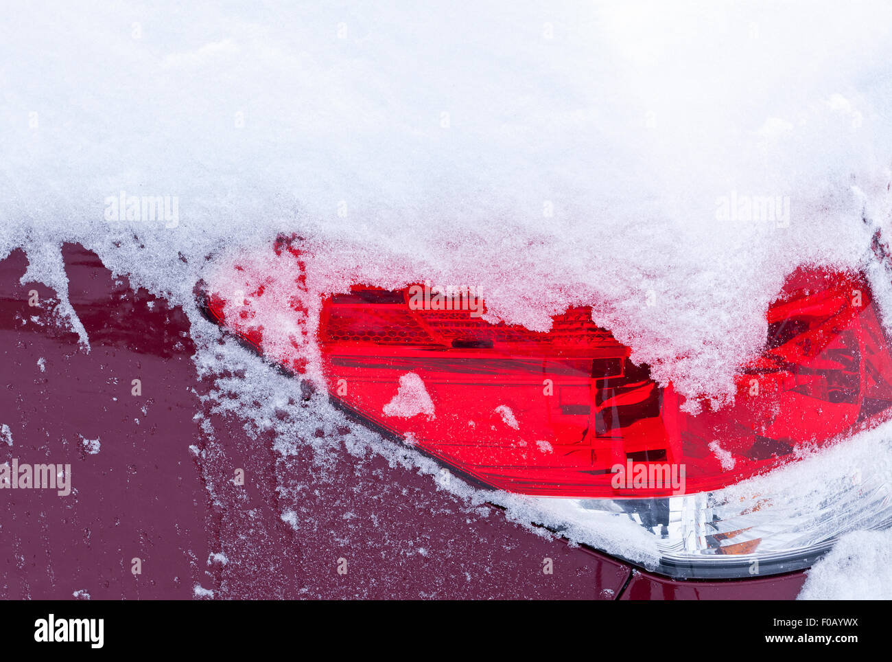 Red taillight, reverse lights and snow on a car covered under white ...
