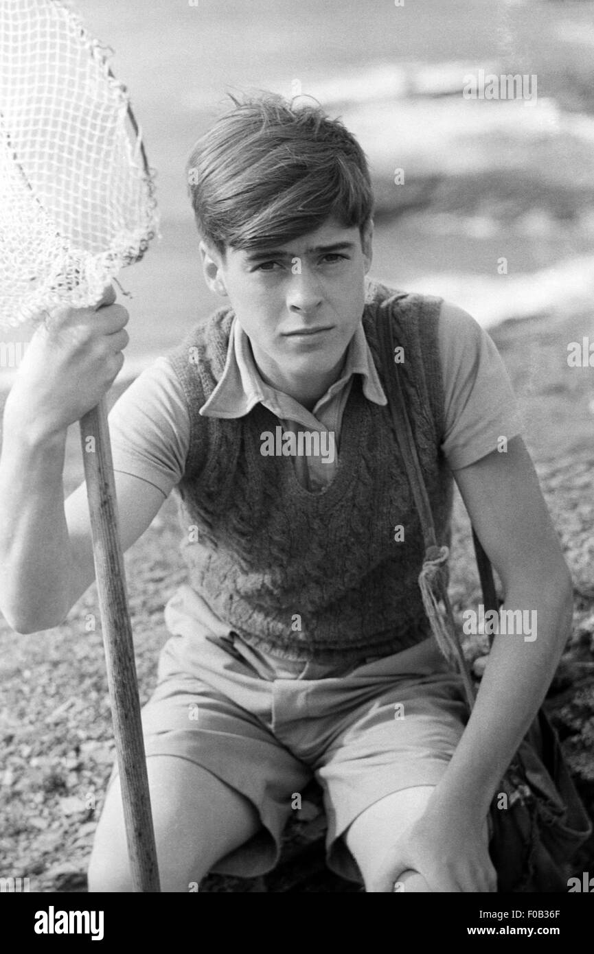 A young man holding a fishing net, sitting on the rocks by the sea ...