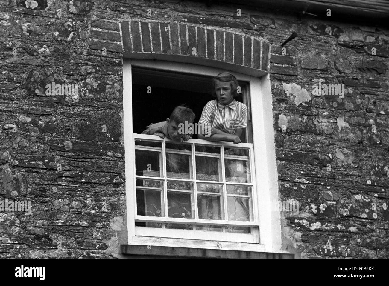 A view from below of a young boy and girl leaning out of an open window ...