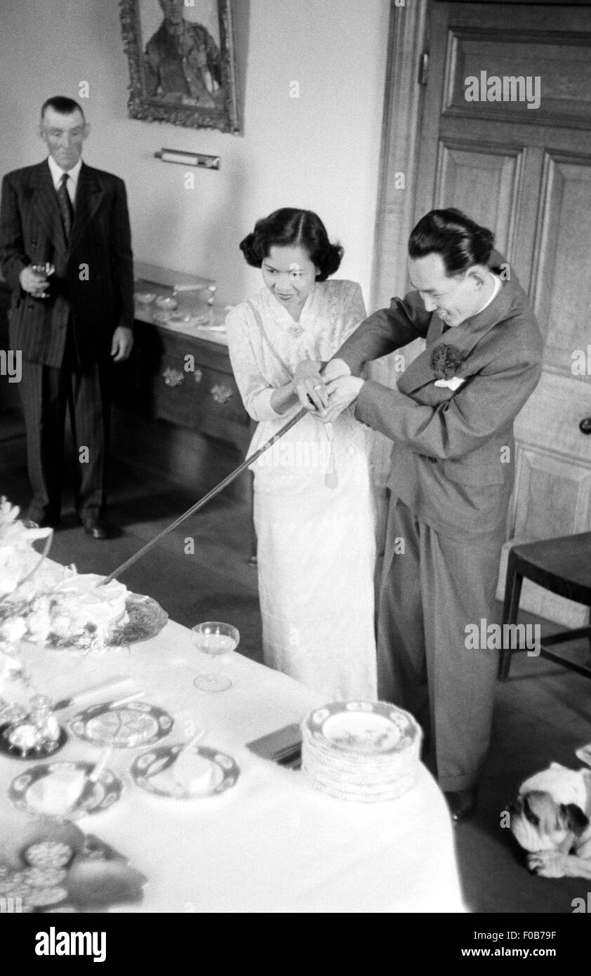 An East Asian couple holding a sword and cutting their wedding cake ...