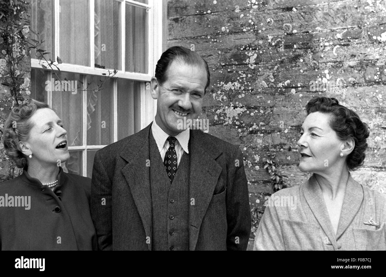 Two middle aged women and a middle aged man standing outside a house ...