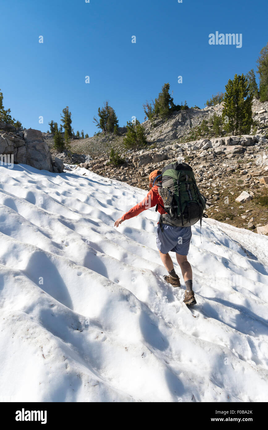 Backpacker hiking up a suncupped snowfield, Wallowa Mountains, Oregon ...