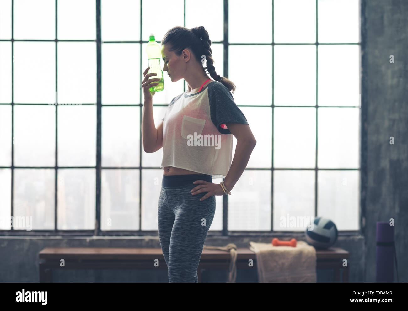 Standing in profile, a woman cools her forehead off with her bottle of ...
