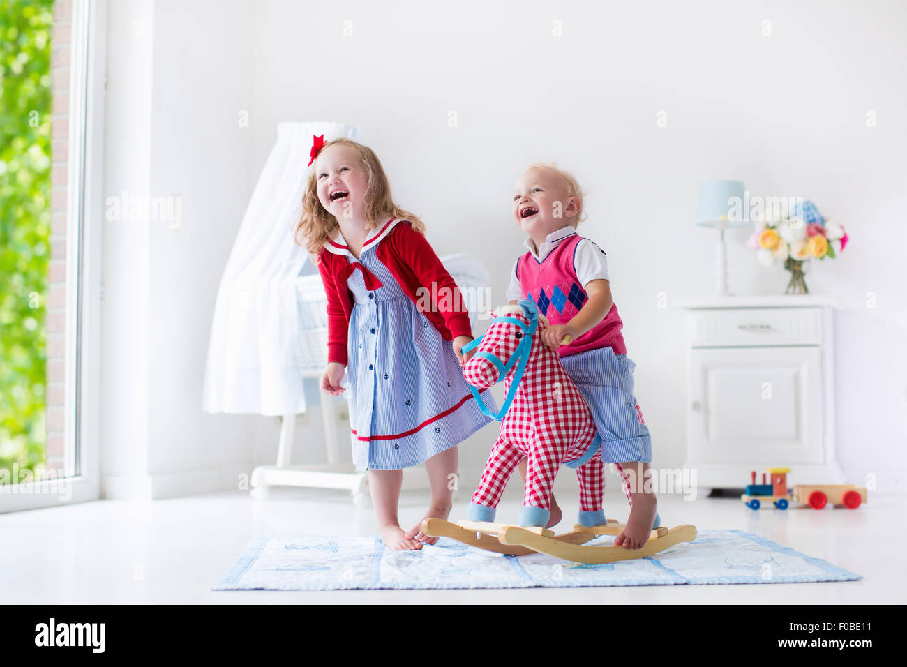 Two children play indoors. Kids riding toy rocking horse. Boy and girl ...