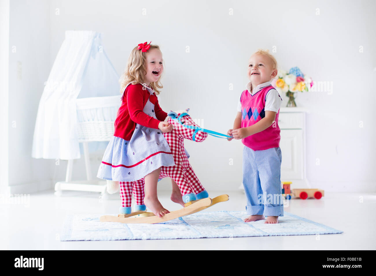 Two children play indoors. Kids riding toy rocking horse. Boy and girl ...