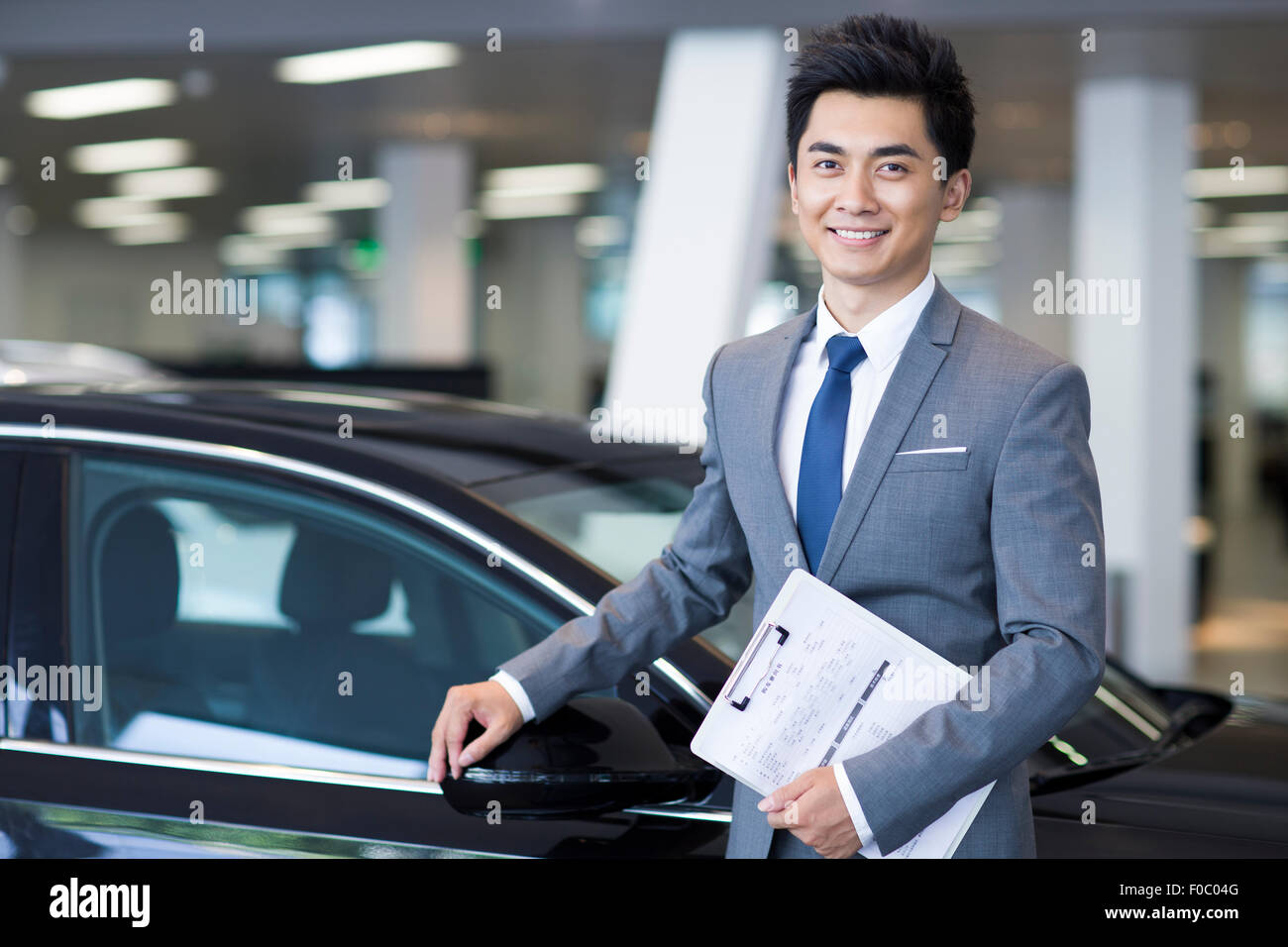 Confident salesman standing with new car in showroom Stock Photo - Alamy