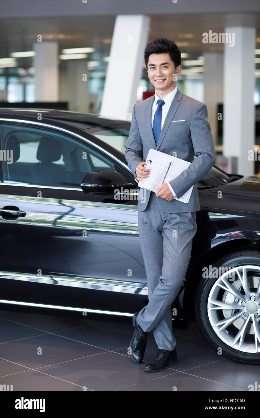 Confident salesman standing with new car in showroom Stock Photo - Alamy