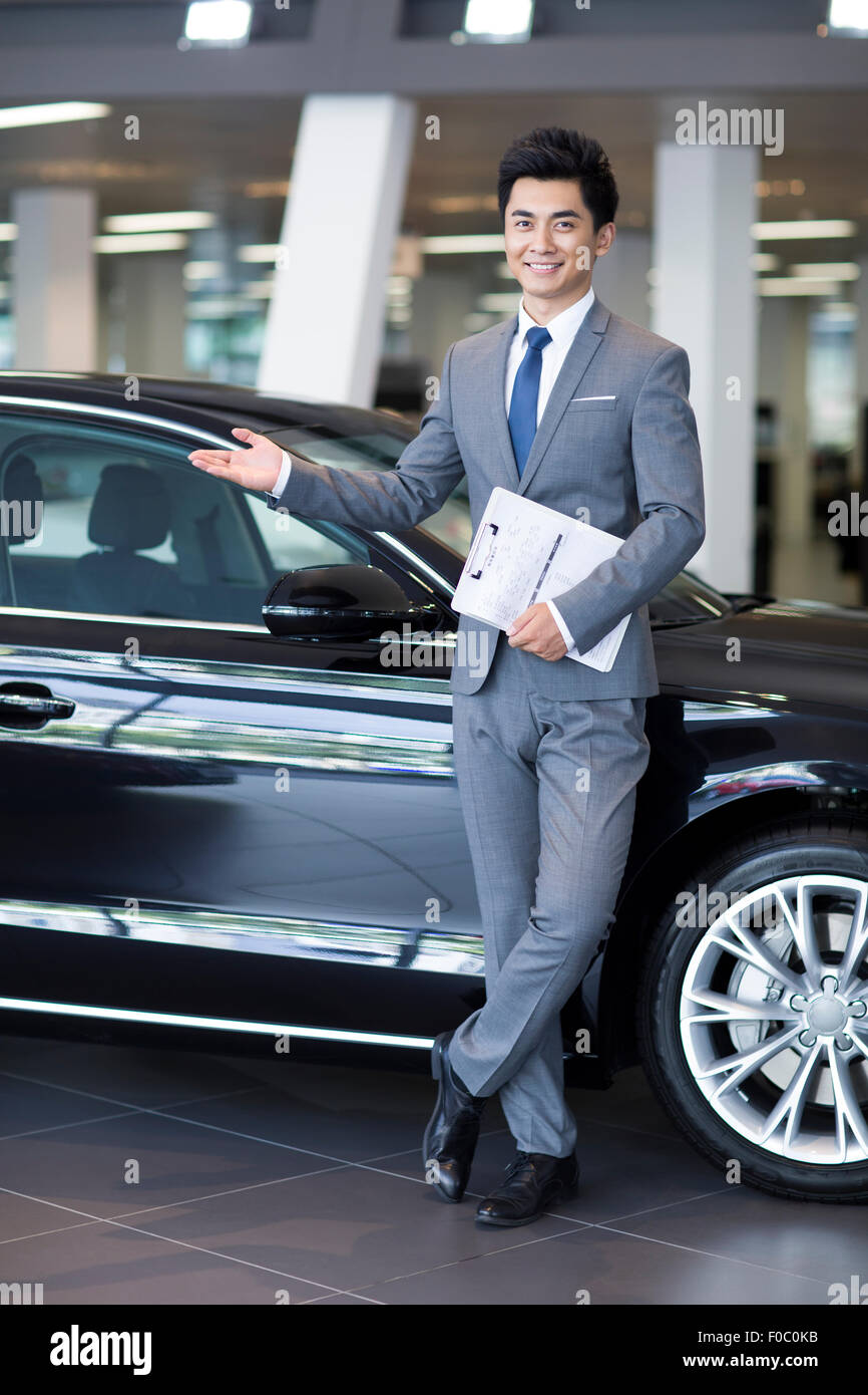Confident salesman standing with new car in showroom Stock Photo - Alamy