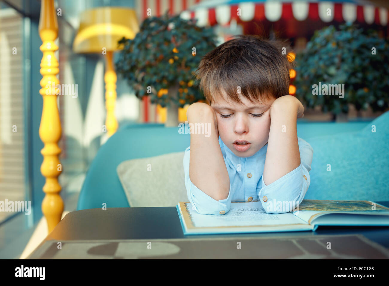 Boring and tired little boy reading book Stock Photo - Alamy