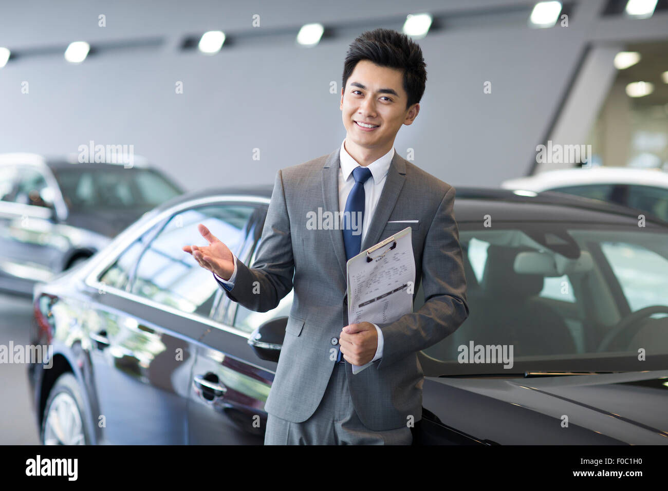 Confident salesman standing with new cars in showroom Stock Photo - Alamy