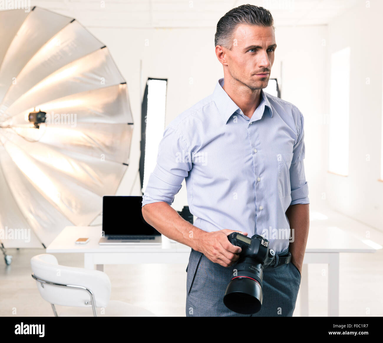 Portrait of a handsome photographer standing with camera in studio ...