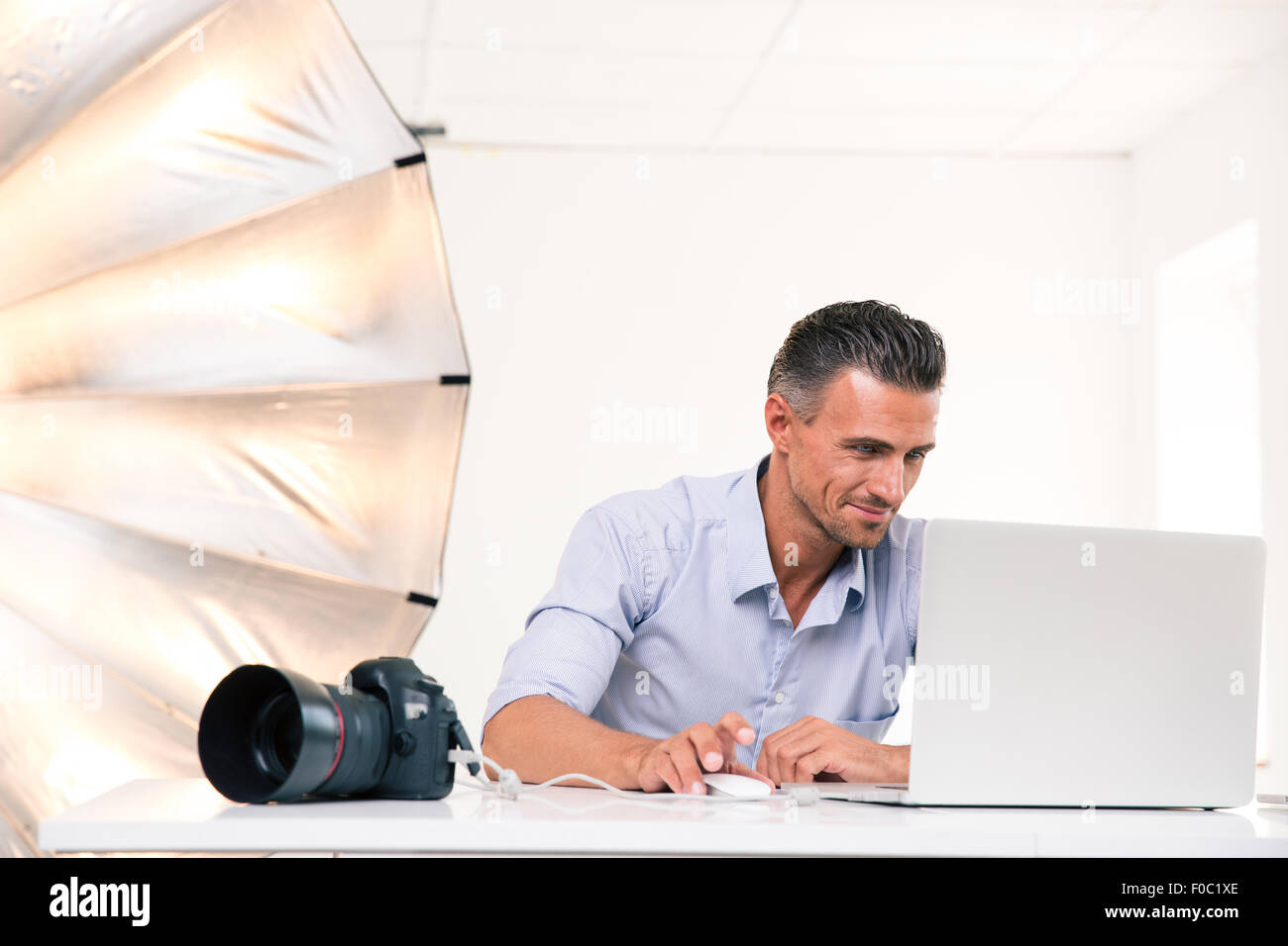 Portrait of a happy photographer using laptop at his workplace Stock ...