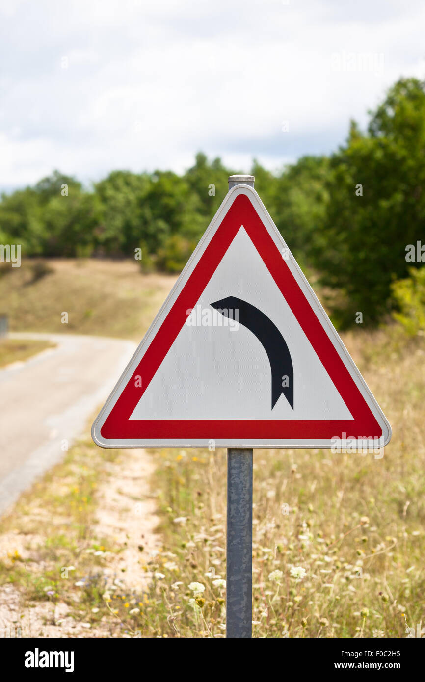 Triangular traffic sign indicating road is turning left on a rural road ...