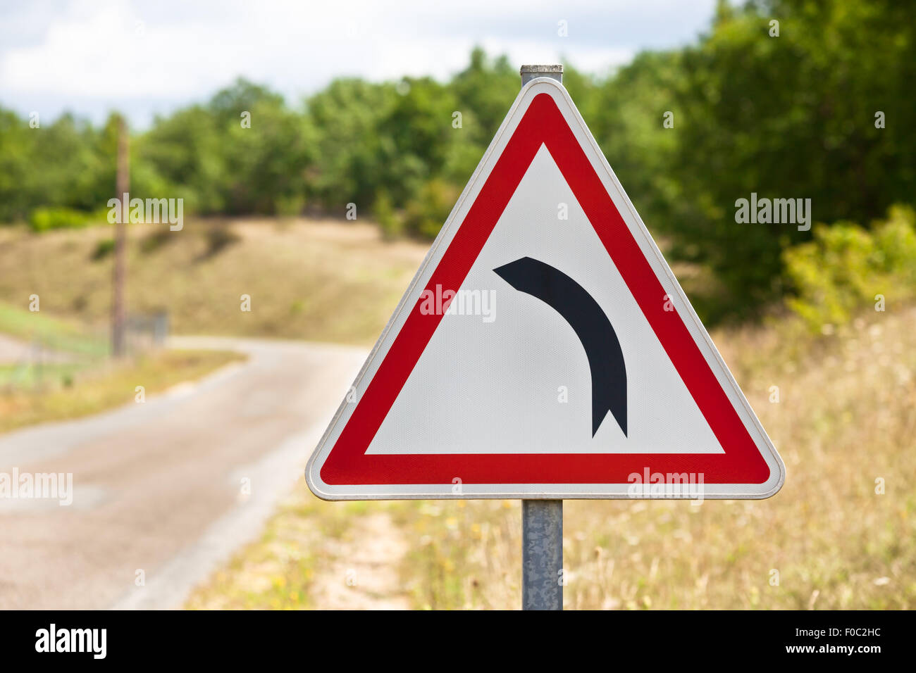 Triangular traffic sign indicating road is turning left on a rural road ...