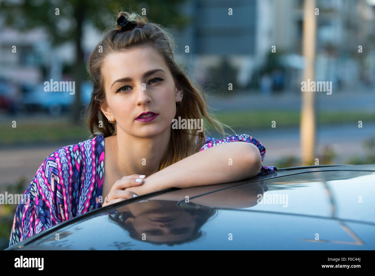 a brunette woman leaning against a car Stock Photo - Alamy