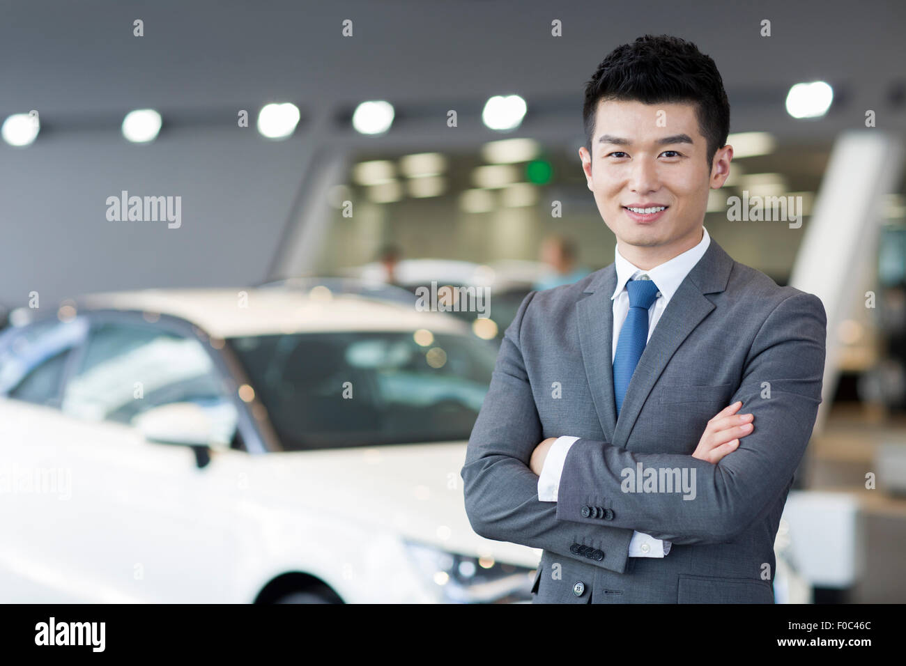 Confident salesman standing with new cars in showroom Stock Photo - Alamy