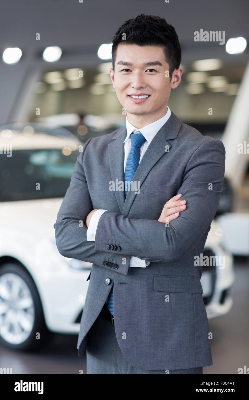Confident salesman standing with new cars in showroom Stock Photo - Alamy