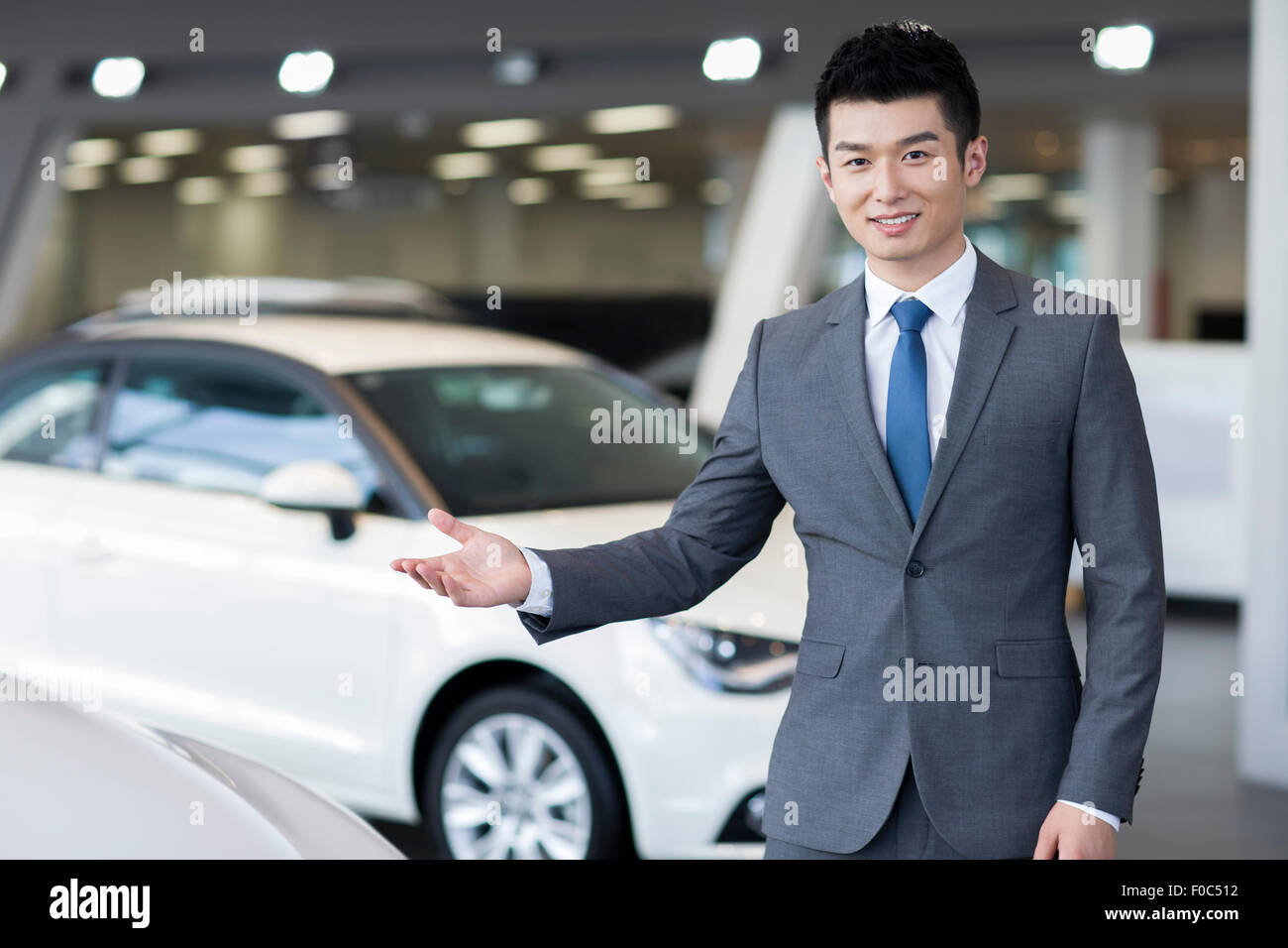 Confident salesman standing with new cars in showroom Stock Photo - Alamy