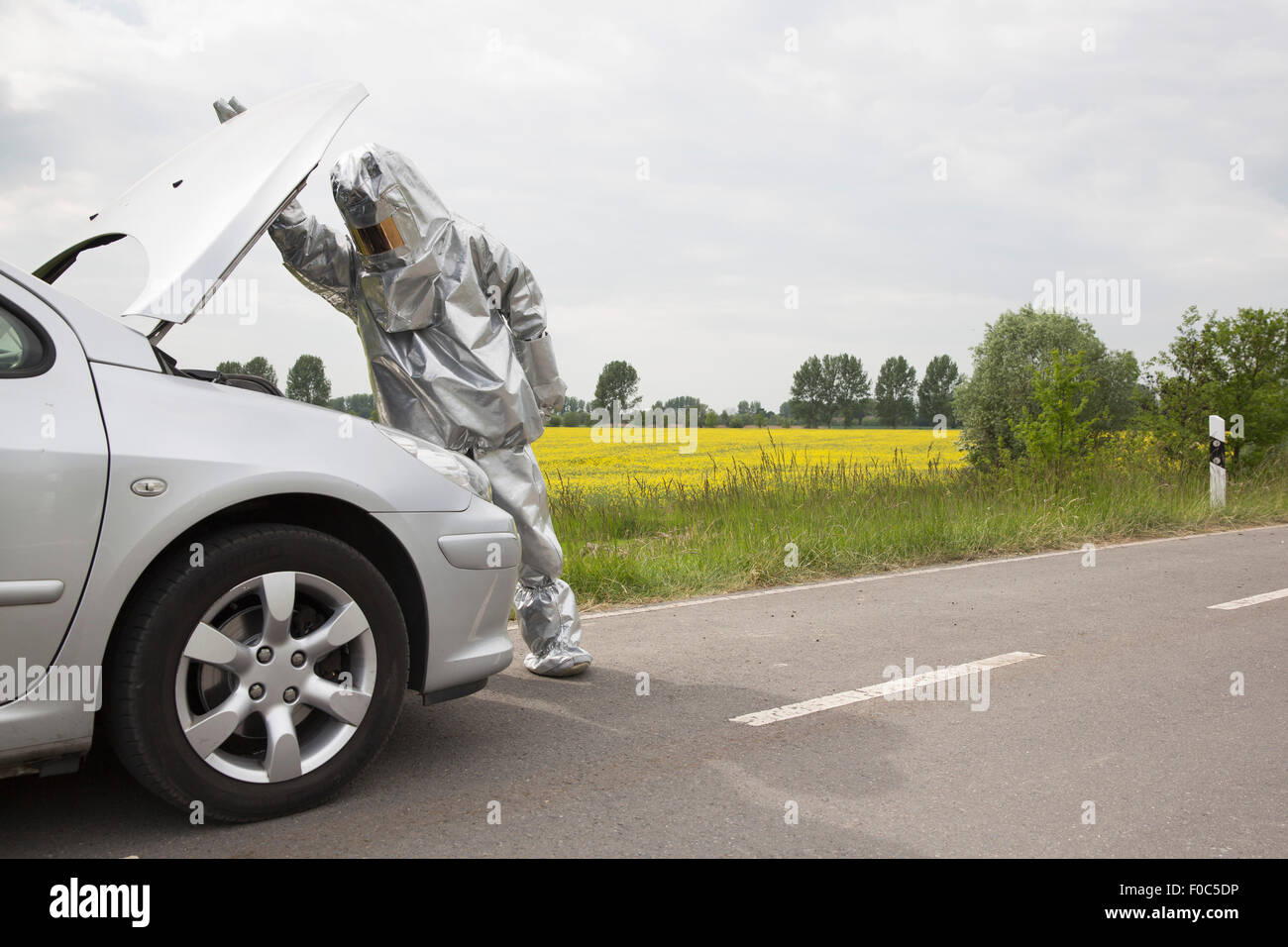 A person in a radiation protective suit looking under the hood of a car ...