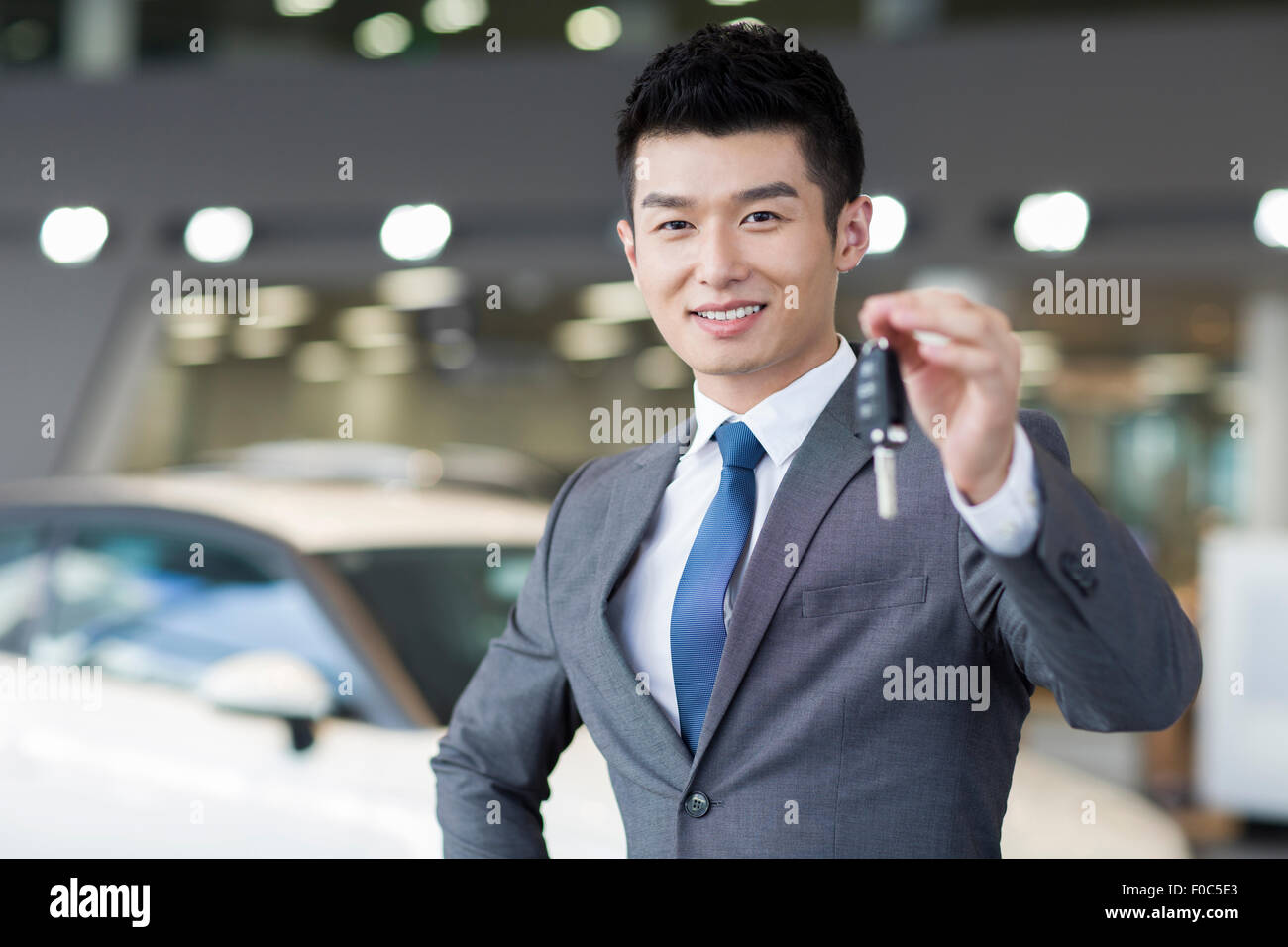 Confident salesman standing with new cars in showroom Stock Photo - Alamy
