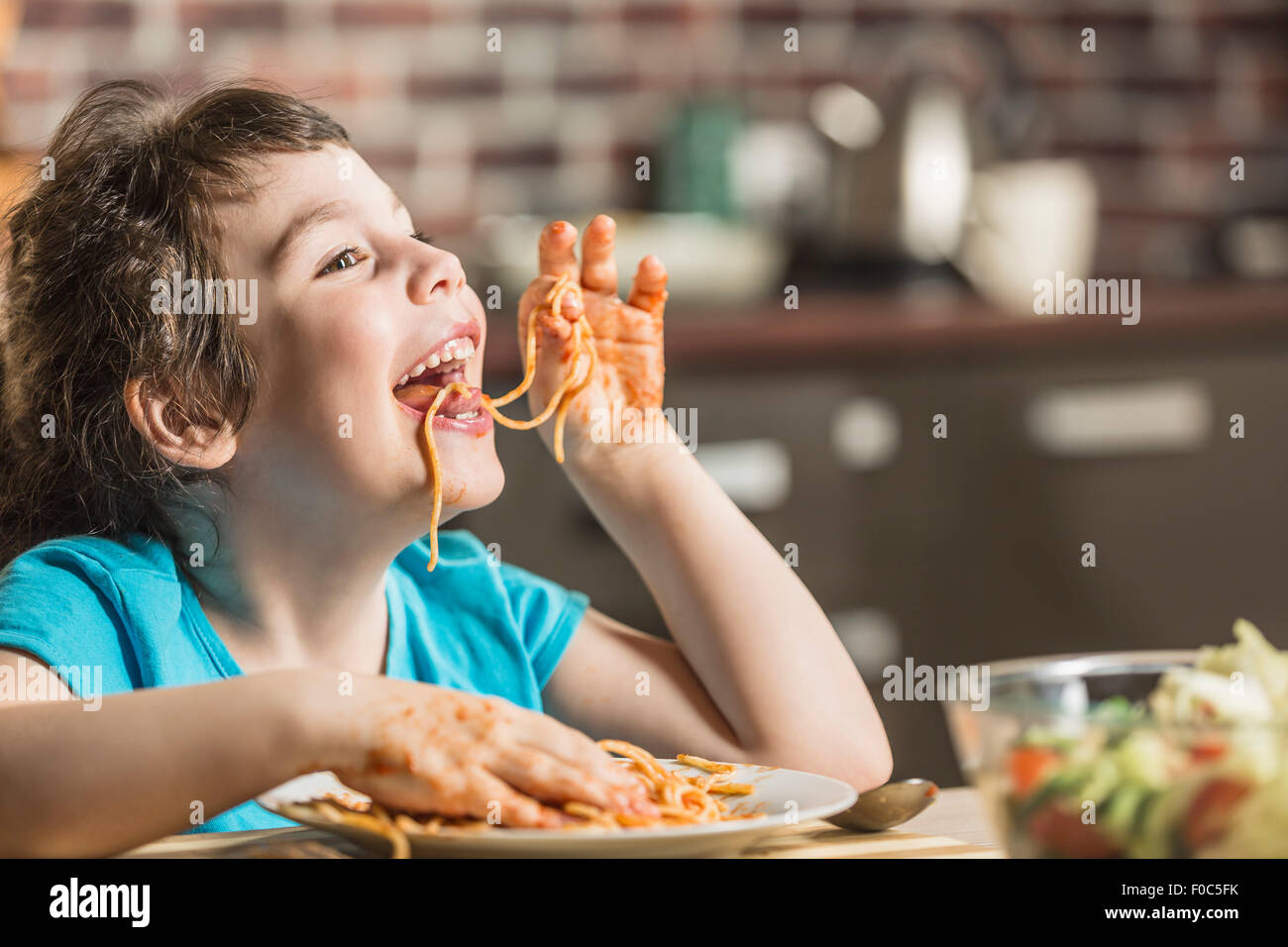 Cheerful little girl eating spaghetti with hands at home Stock Photo ...