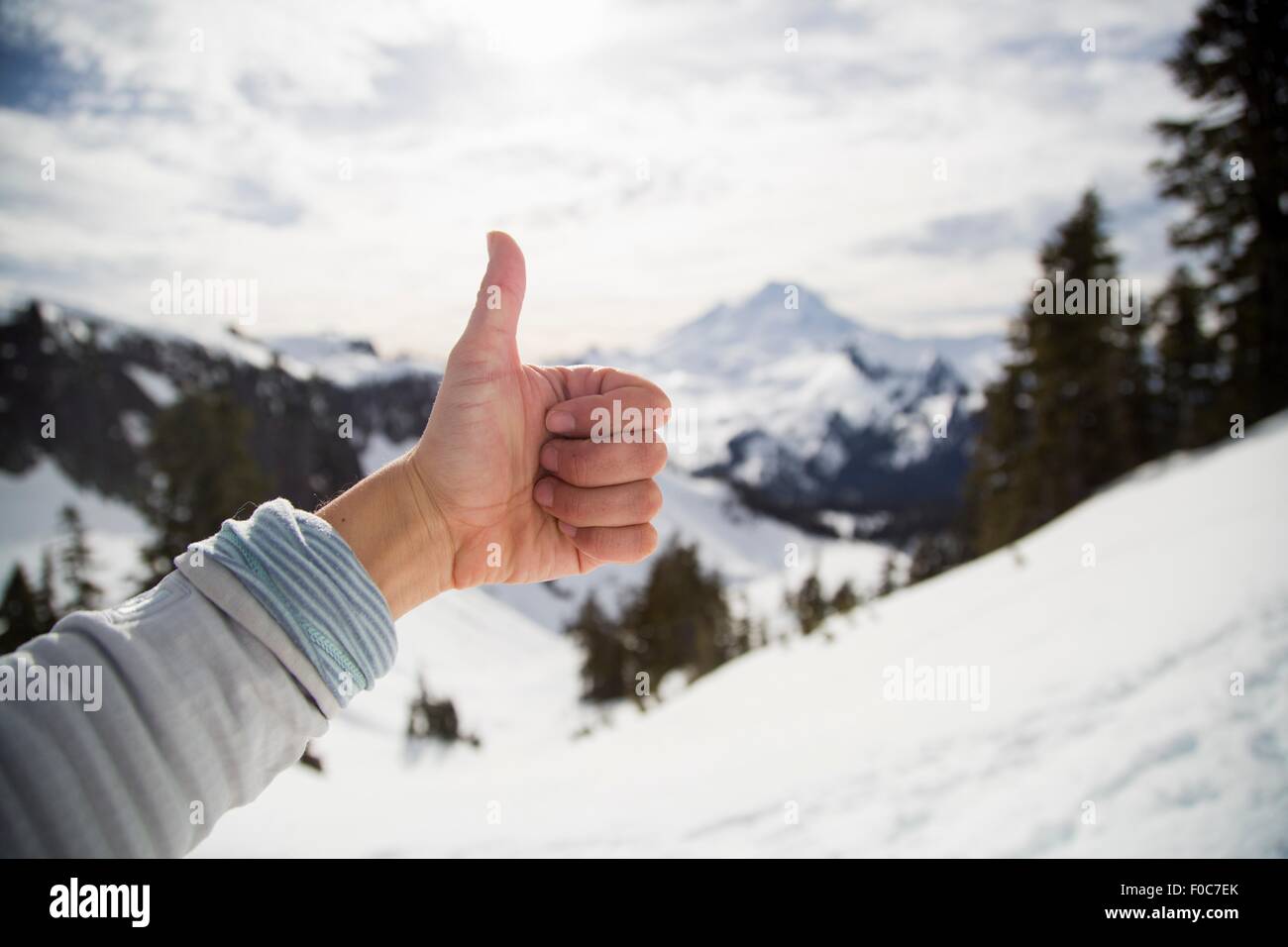 Female hand making thumbs up in front of snow covered view, Mount Baker ...
