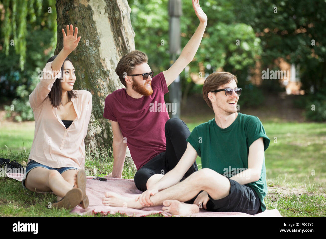Happy friends waving while relaxing at park Stock Photo - Alamy