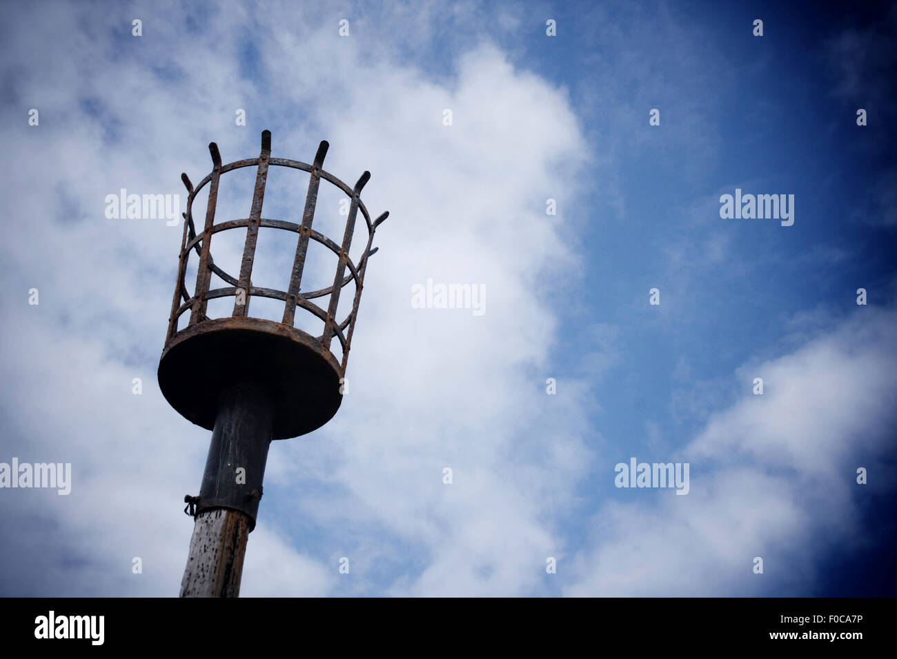 Rusty beacon brazier in silhouette against blue sky on seafront ...