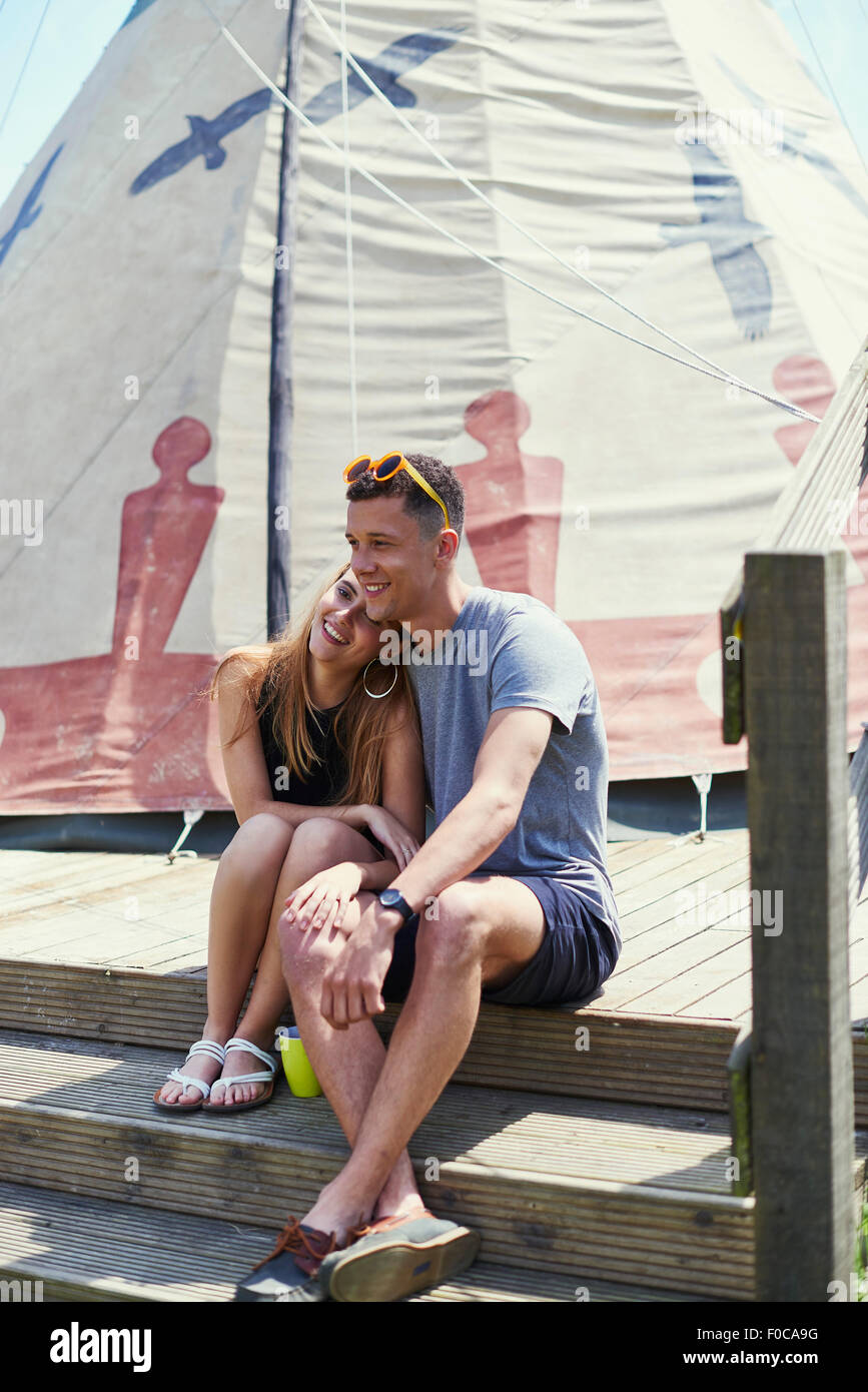 Happy young couple sitting on teepee structure while glamping Stock ...